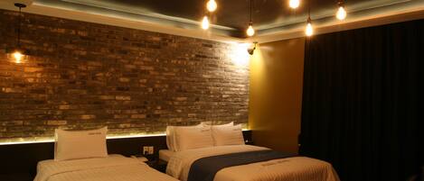 Quarto de hotel com duas camas, parede de tijolos e luminárias suspensas.