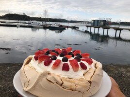 Uma sobremesa pavlova num prato, com vista para a água ao fundo.