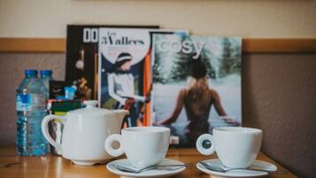 Uma mesa de madeira com duas chávenas brancas, um bule, uma garrafa de água e revistas.
