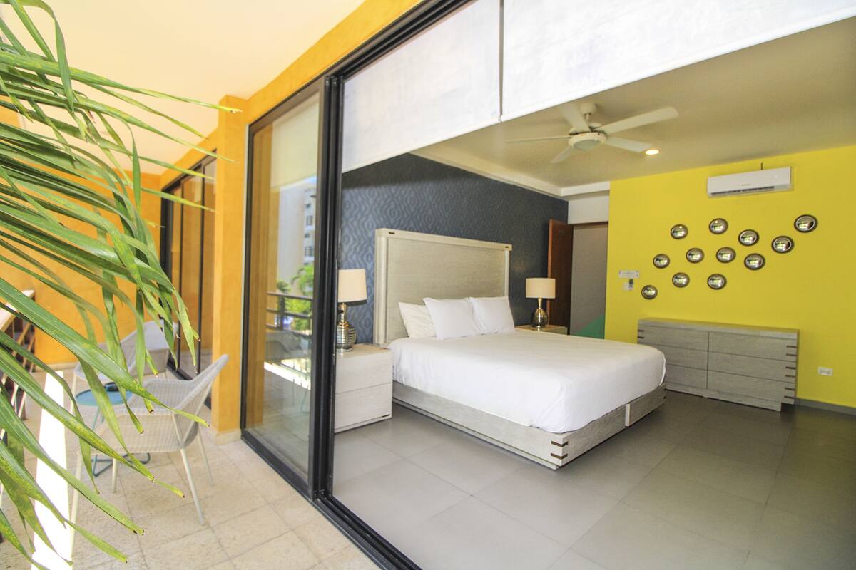 Quarto com cama, mesas de cabeceira, ventoinha no teto e parede decorada com detalhes circulares.