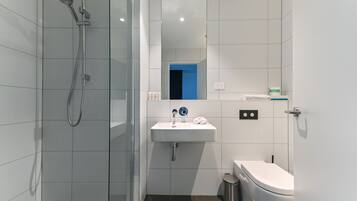 Uma casa de banho moderna com cabine de chuveiro em vidro, lavatório branco com espelho e sanita.