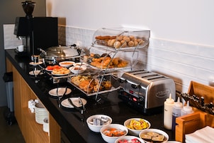 Disposição de buffet com diversos alimentos, uma máquina de café e uma torradeira.