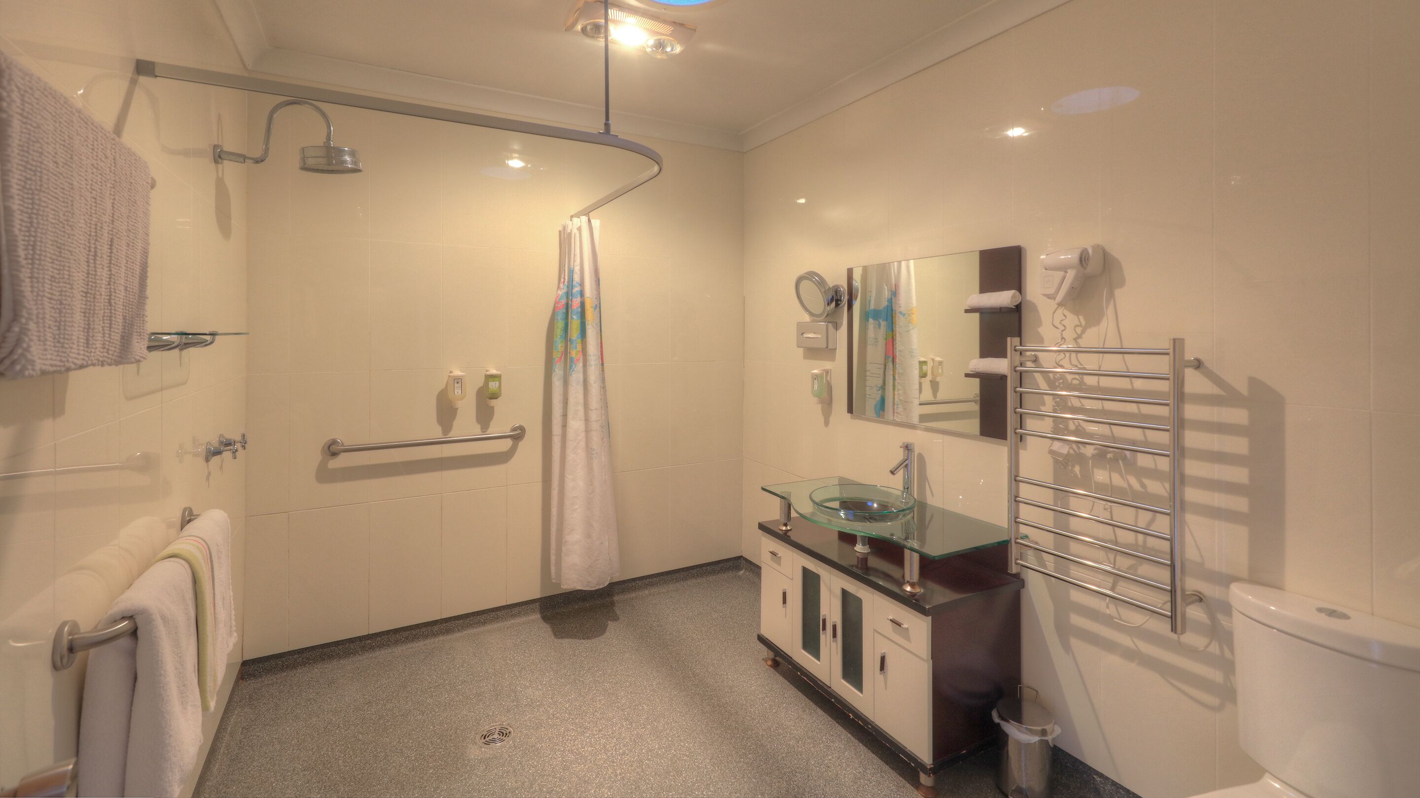 Uma casa de banho moderna com lavatório de vidro, chuveiro com chuveiro manual, porta-toalhas e sanita.
