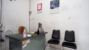 Uma área de recepção com balcão, cadeiras, um calendário e um telefone fixado na parede.