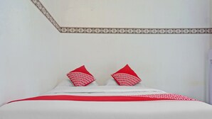 Cama com roupa de cama branca e duas almofadas vermelhas com desenhos brancos.