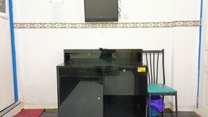 Quarto com armário preto, televisão na parede, uma cadeira e uma pequena mesa com uma bolsa roxa.