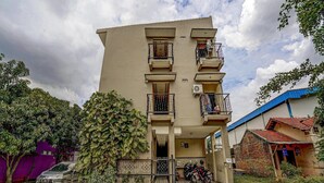 Um edifício de vários andares com varandas, um carro estacionado na frente e uma motocicleta do lado de fora.