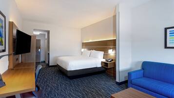 Quarto de hotel com cama, escrivaninha, cadeira, sofá e televisão.