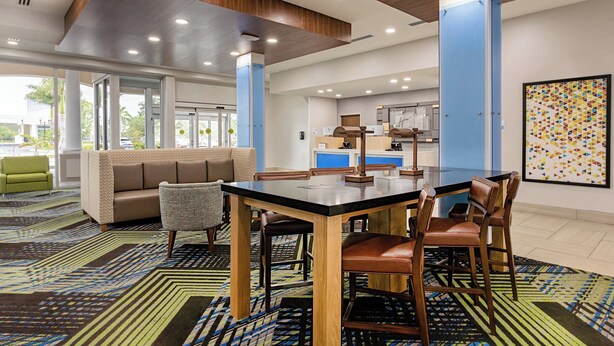 Um hall de hotel com área de refeições, um sofá e cozinha ao fundo.