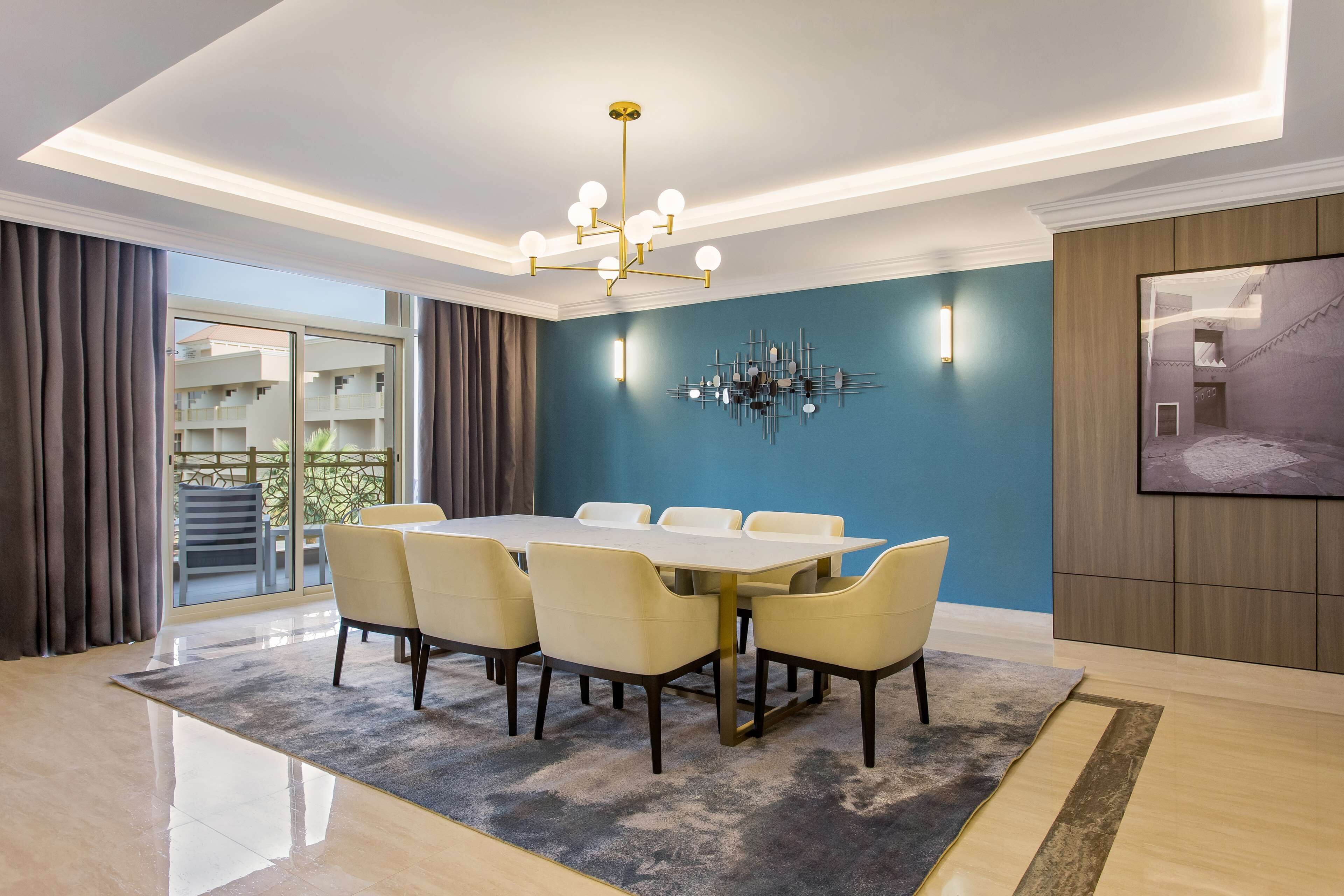 Uma sala de jantar moderna com uma mesa grande e cadeiras, um candelabro e vista para uma varanda.