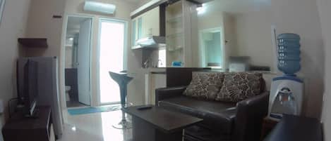 Uma sala de estar com sofá, mesa de centro, televisão e dispensador de água.