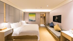 Quarto de hotel com cama, mesa de cabeceira, televisão de tela plana na parede, sofá e pequena escrivaninha com cadeira.
