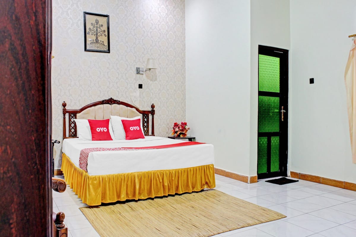 Quarto com cama, cabeceira de madeira, ar-condicionado fixado na parede, quadro emoldurado e porta verde.