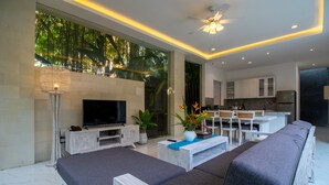 Uma sala de estar moderna com televisão, sofá, mesa de centro e uma área de jantar com cadeiras e mesa.