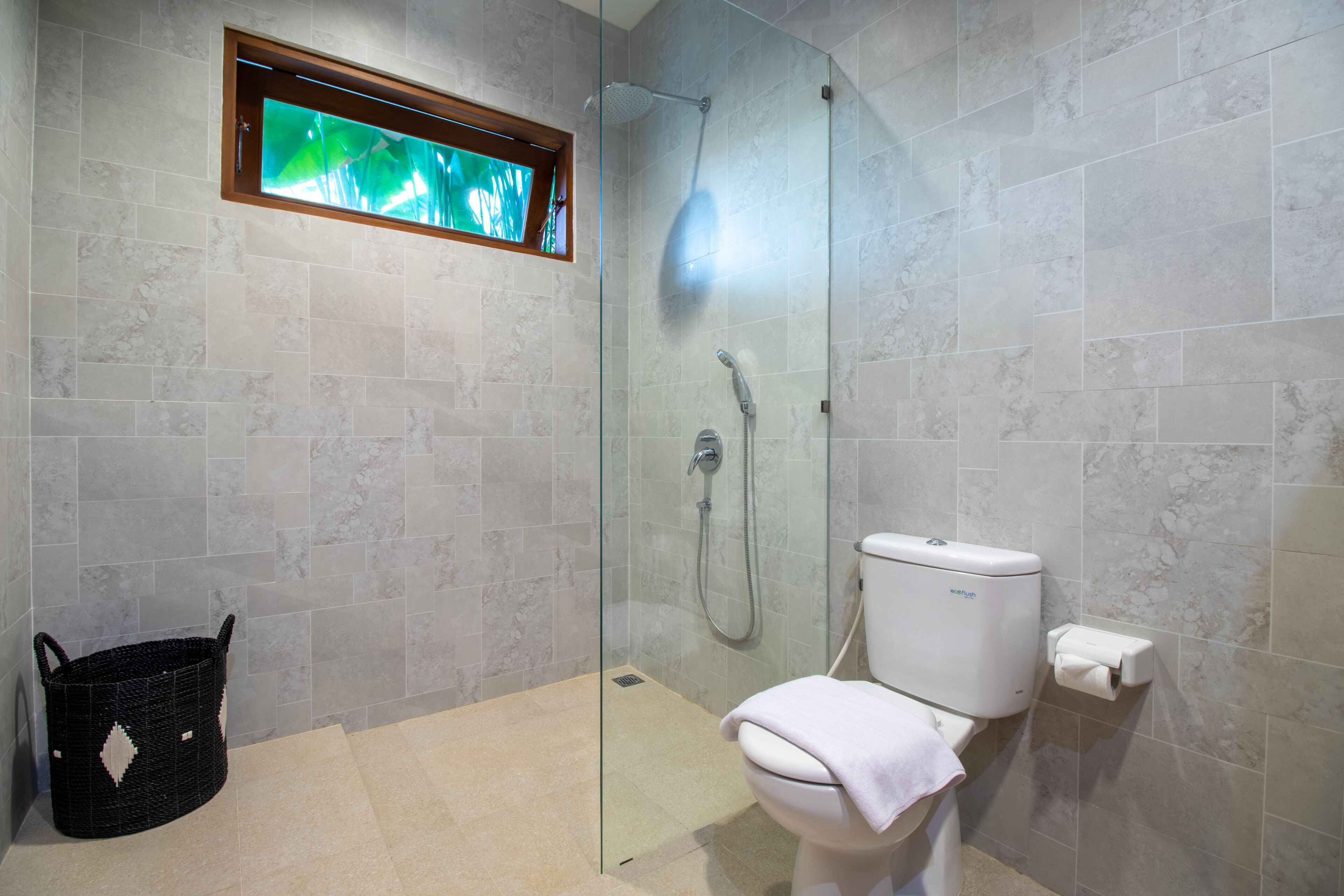 Uma casa de banho moderna com cabine de duche em vidro, sanita e uma pequena janela.