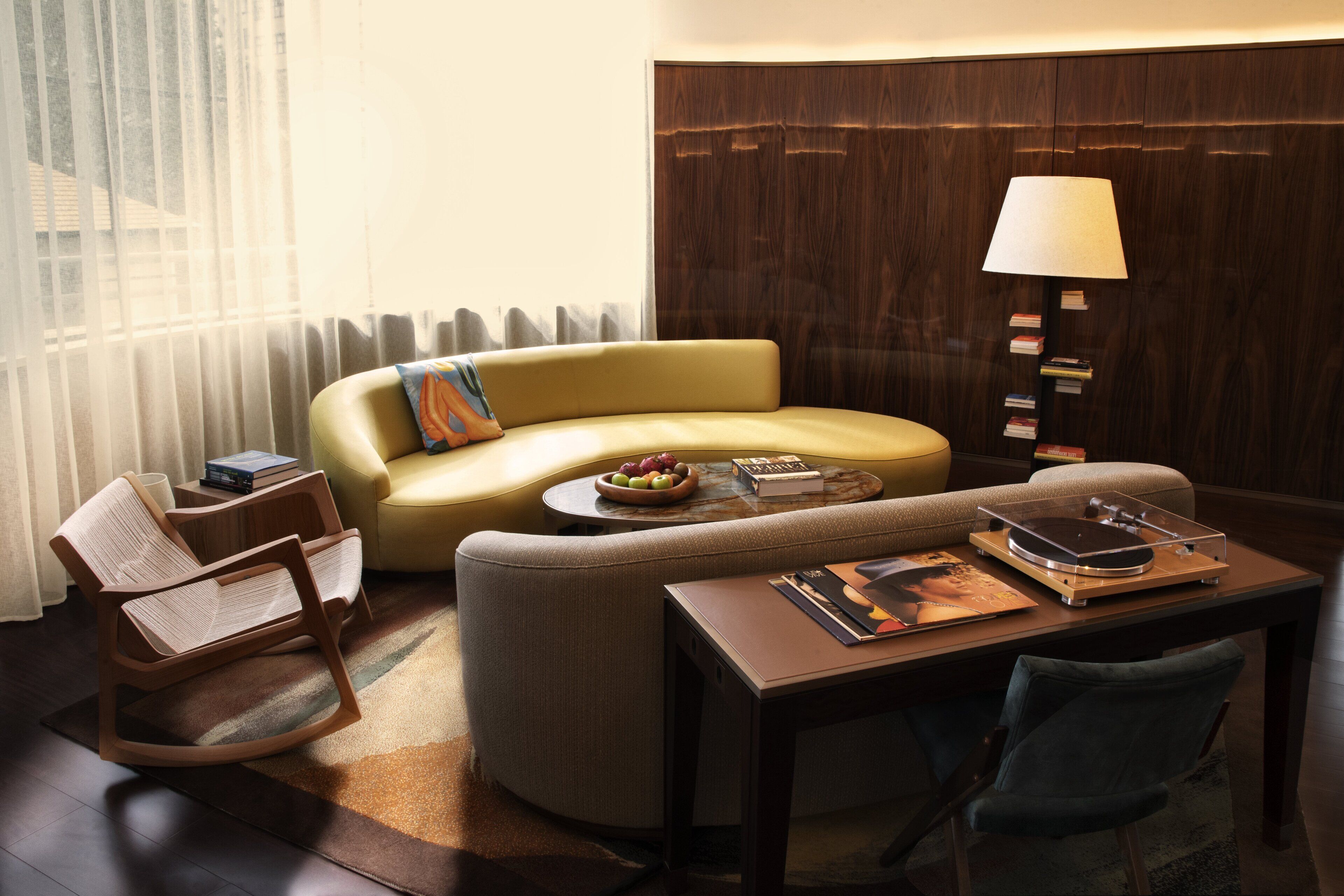 Uma sala de estar moderna com sofá, mesa de centro, mesa lateral com livros, abajur e uma poltrona.