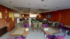 Um restaurante espaçoso com várias mesas e cadeiras, um bar e vista panorâmica da cidade através de grandes janelas.
