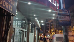 Exterior do Hotel Adali, com uma placa bem visível, entrada aparente e placa indicando estacionamento próximo.