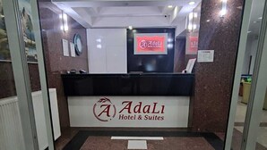 A área de recepção do AdaLi Hotel & Suites, com piso de mármore, balcão de atendimento e placa na parede.