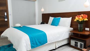 Quarto de hotel moderno com uma cama bem arrumada, mesa de cabeceira com um vaso de flores e um pequeno armário com tomada.