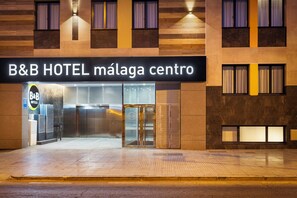 Entrada de hotel com uma placa indicando 'B&B HOTEL málaga centro', porta de vidro e escadaria de metal que leva à entrada.