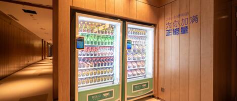 Um corredor com duas máquinas de venda automática repletas de bebidas e lanches, painéis de madeira nas paredes e uma placa com caracteres chineses.