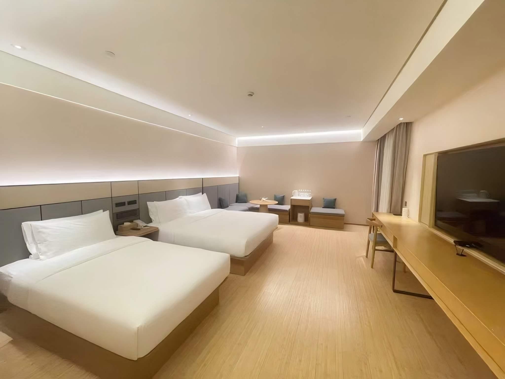 Quarto de hotel com duas camas, uma escrivaninha, uma cadeira, televisão e mesa de cabeceira com abajur.