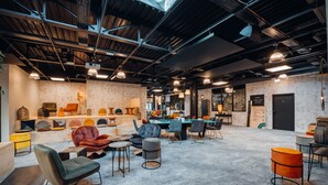 Decoração moderna com pé direito alto, iluminação industrial e diversas opções de assento, incluindo sofás e cadeiras.