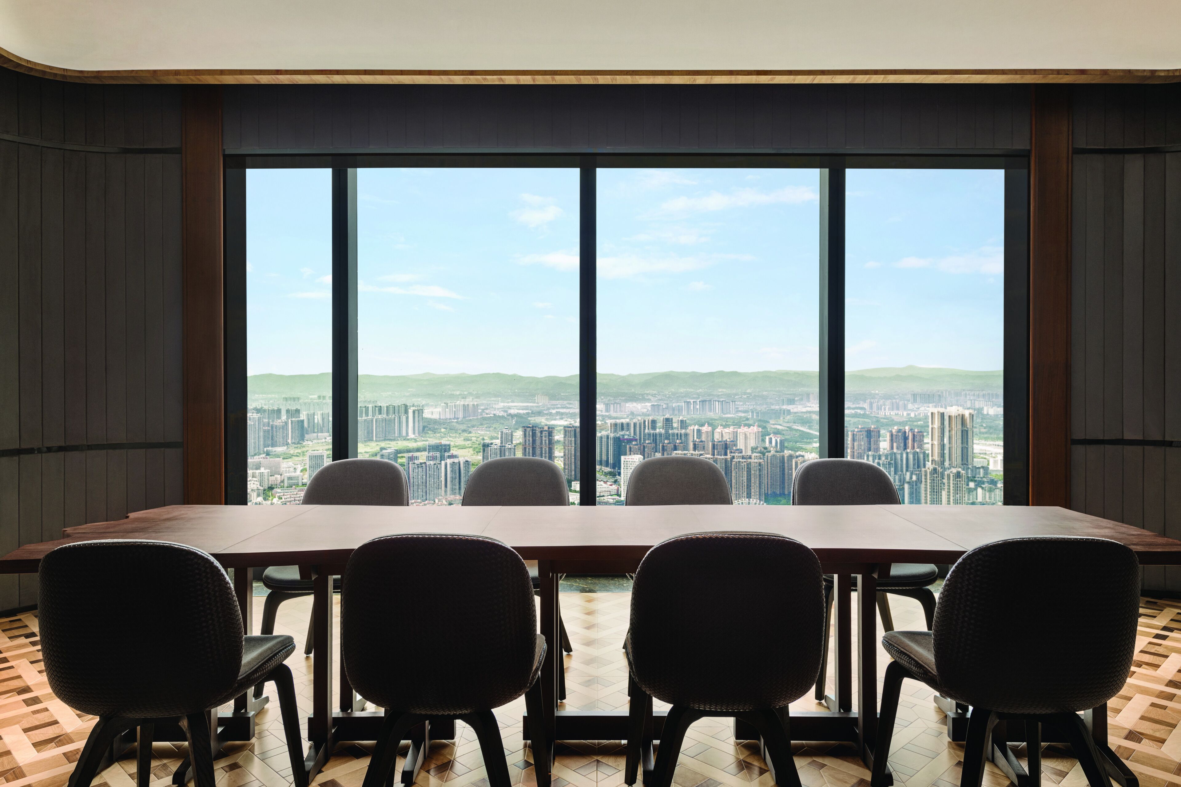 Sala de conferências com uma mesa grande e seis cadeiras, janelas amplas com vista para a cidade.