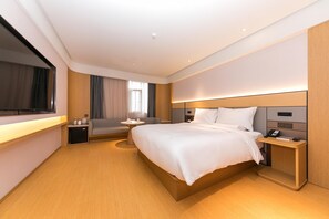 Quarto de hotel com cama grande, mesas de cabeceira, televisão e área de estar.