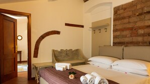 Quarto de hotel com cama, cabeceira de madeira, parede de tijolo e porta que dá para outro cômodo.