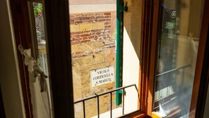 Uma janela com vista para um muro de tijolos e uma placa que diz 'VICOLLO CORTICELLA S. MARCO'.
