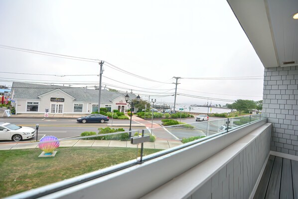 Uma varanda com vista para a rua, um edifício com uma placa e uma área gramada com uma escultura.