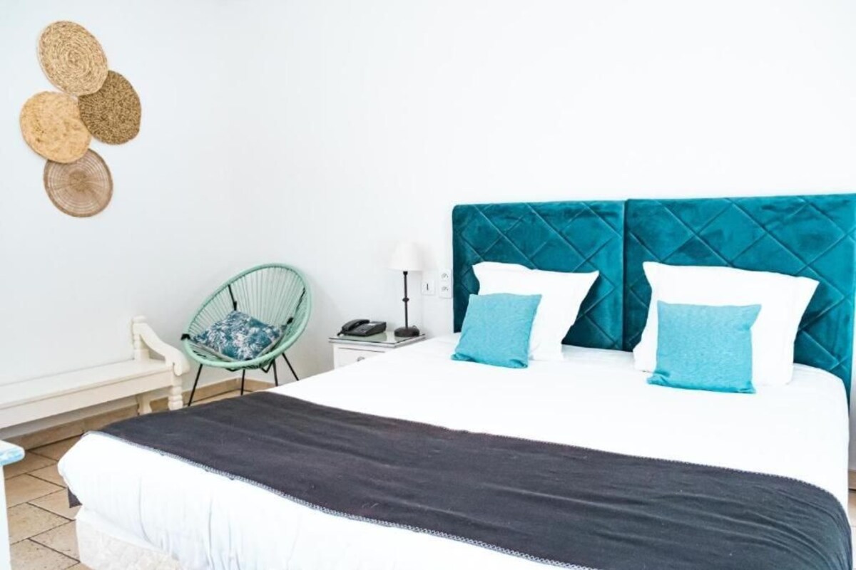 Uma cama com cabeceira acolchoada, uma mesa de cabeceira com abajur, uma cadeira e um painel de parede com arte em tecido.
