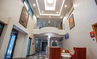 Um saguão de hotel com teto alto, luminária central e uma varanda com corrimão, além de uma placa indicando um restaurante.