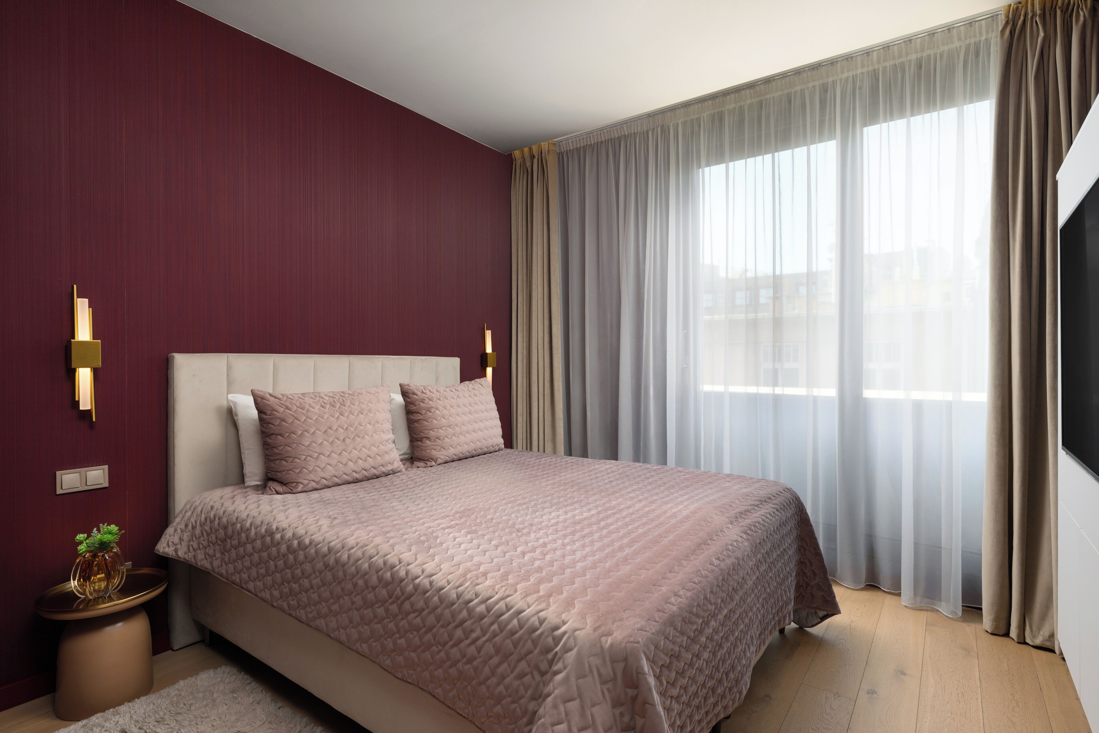 Quarto com cama, cortinas e luminária fixada na parede.