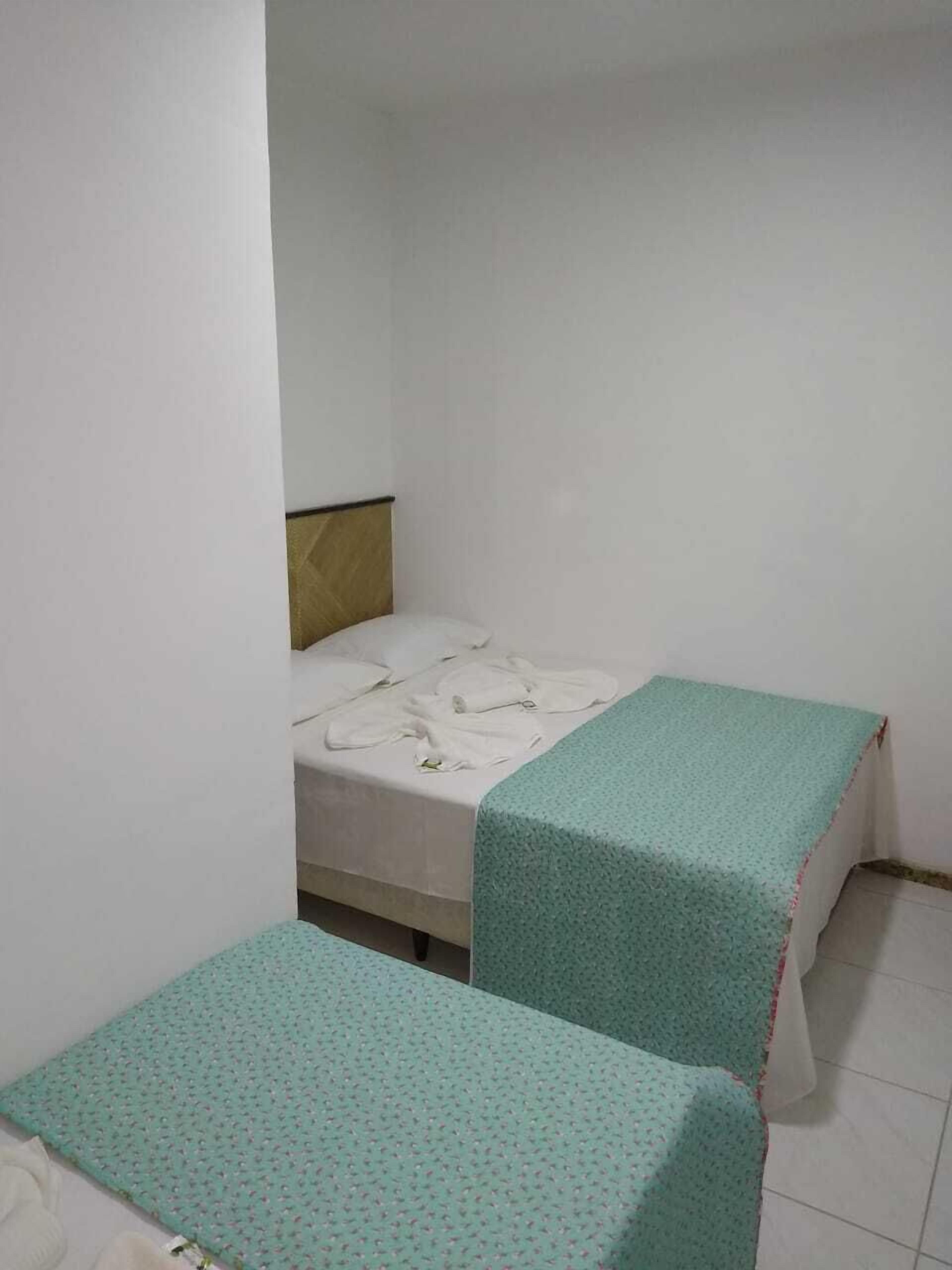 Quarto pequeno e pouco mobiliado, com uma cama e duas mesas de cabeceira.