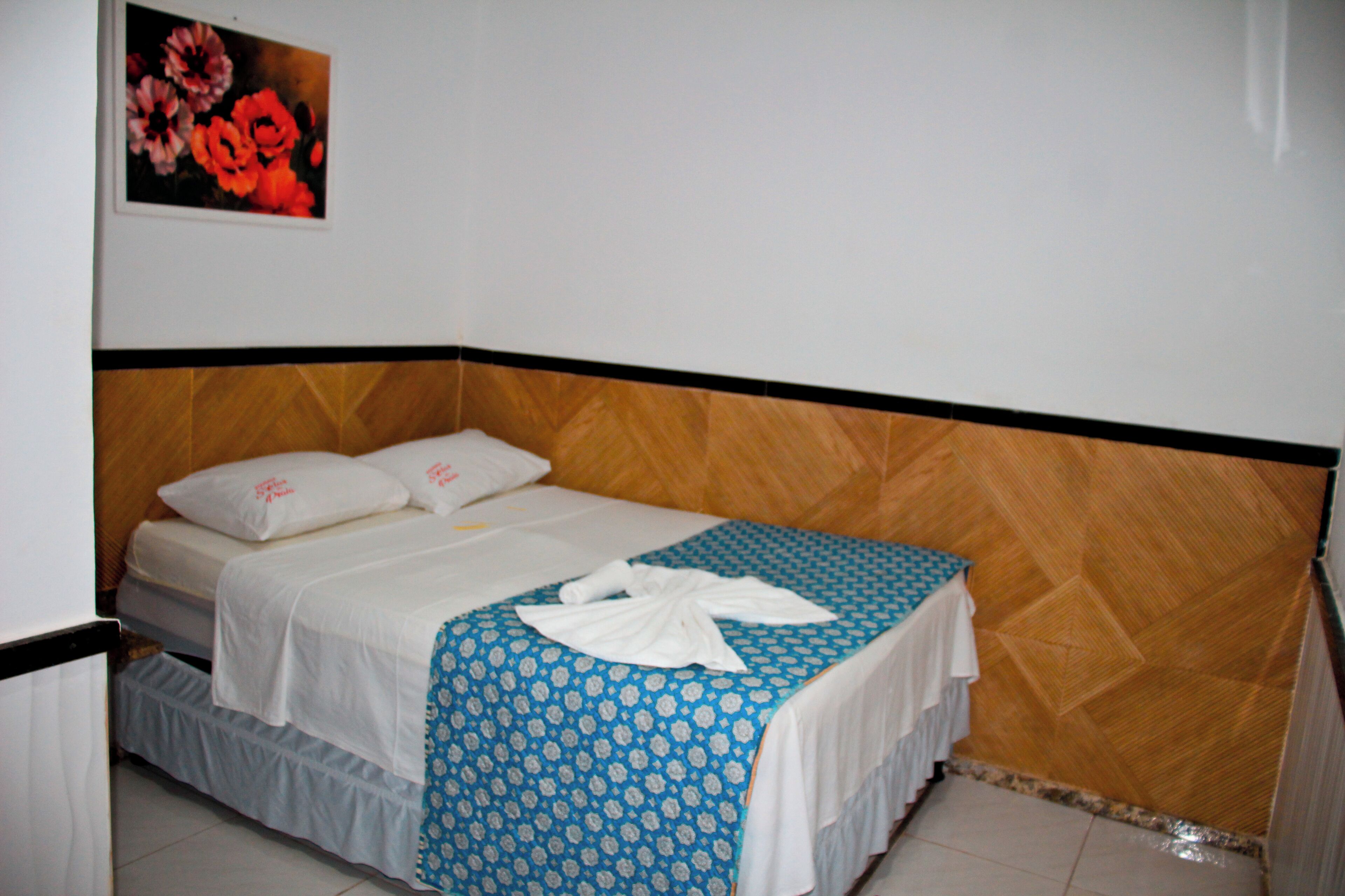 Quarto de hotel com uma cama, cabeceira de madeira e um quadro de flores na parede.