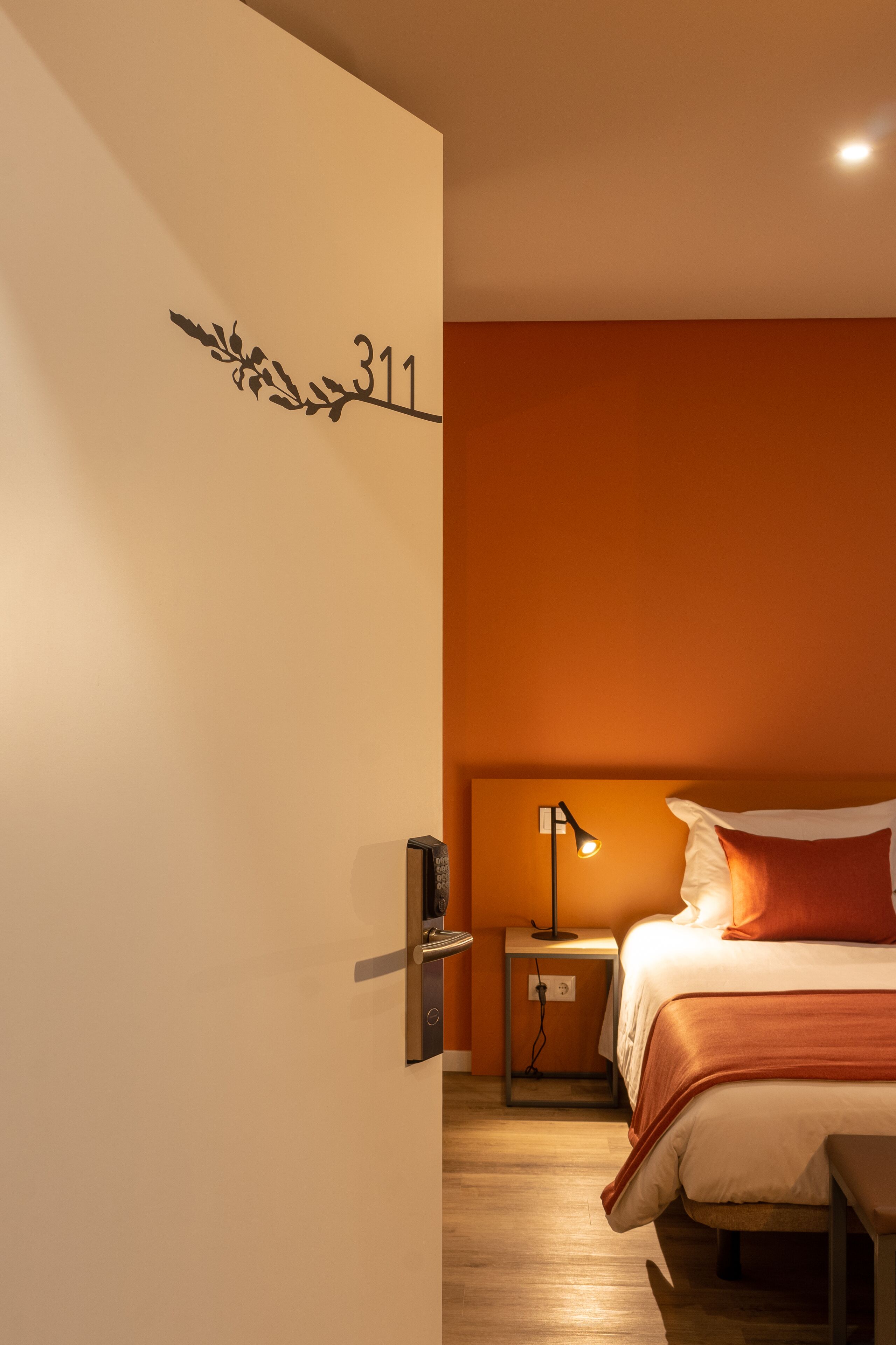 Quarto de hotel com cama, mesa de cabeceira, abajur e parede com sinal de número.