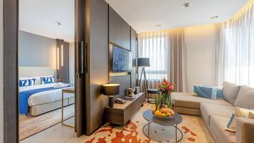 Quarto de hotel moderno com cama, sofá, mesa de centro e TV na parede.