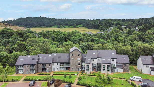 Edifício residencial com vários apartamentos, cercado por vegetação exuberante e uma paisagem montanhosa.