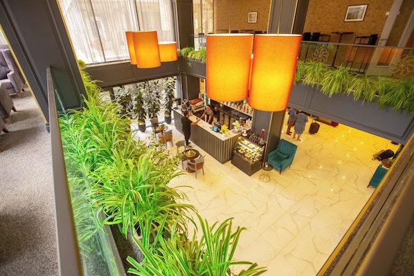 Um saguão de hotel com área de bar central, assentos e uma grande instalação de plantas em interior.