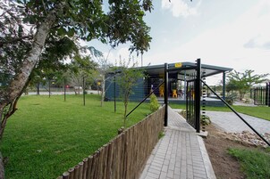 Uma área externa cercada, com um caminho pavimentado que leva a uma construção coberta.