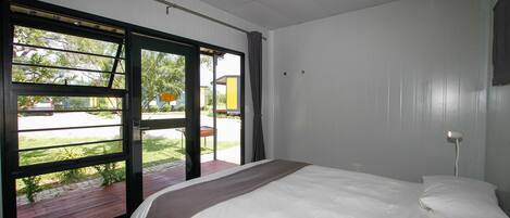 Quarto com cama, janela e porta que dá para área externa.