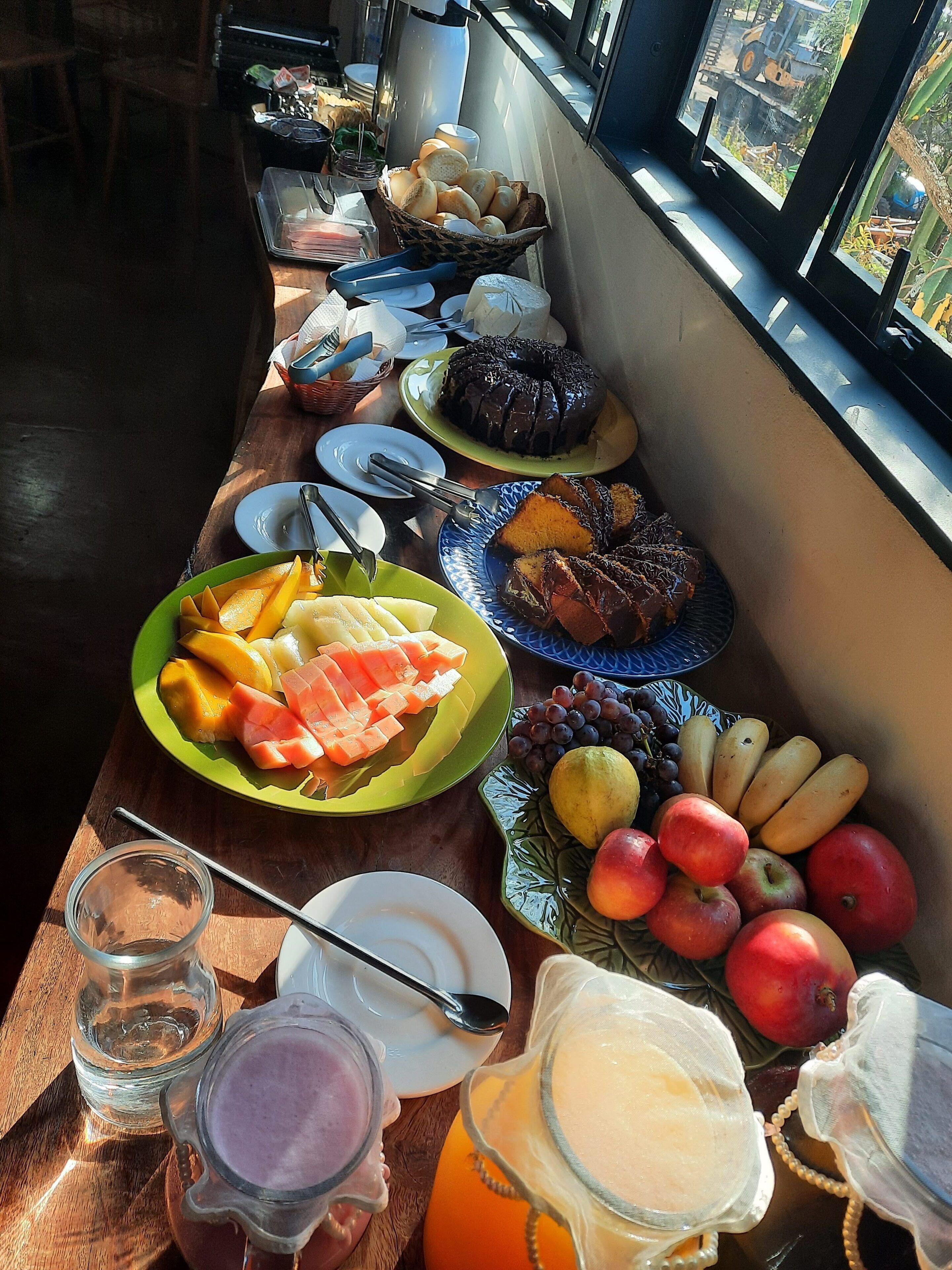 Um buffet de café da manhã com diversas frutas, doces e bebidas.
