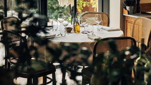 Uma área de refeições com uma mesa posta para quatro pessoas, janelas amplas e uma luminária pendente.
