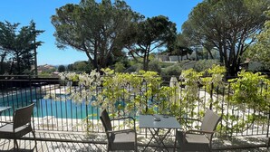Um deck de madeira com cadeiras de vime e uma mesa, com vista para uma piscina rodeada por árvores e vegetação.