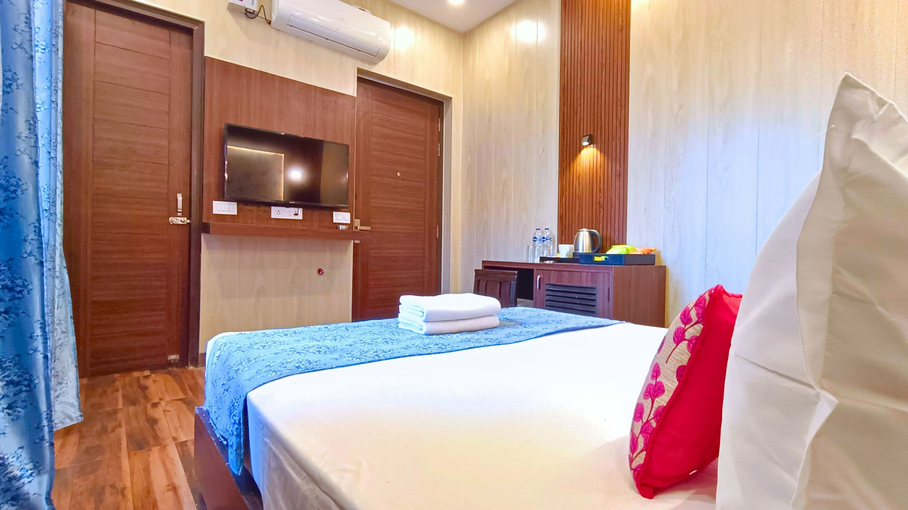 Quarto de hotel com cama, televisão na parede, escrivaninha com espelho e guarda-roupa.