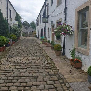 Uma rua de paralelepípedos ladeada por edifícios brancos, alguns com cestos de flores e plantas em vasos.