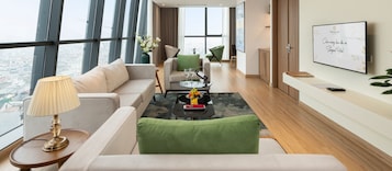Uma sala de estar moderna com sofá, poltrona e mesa de centro, uma janela grande com vista para a cidade e uma TV na parede.